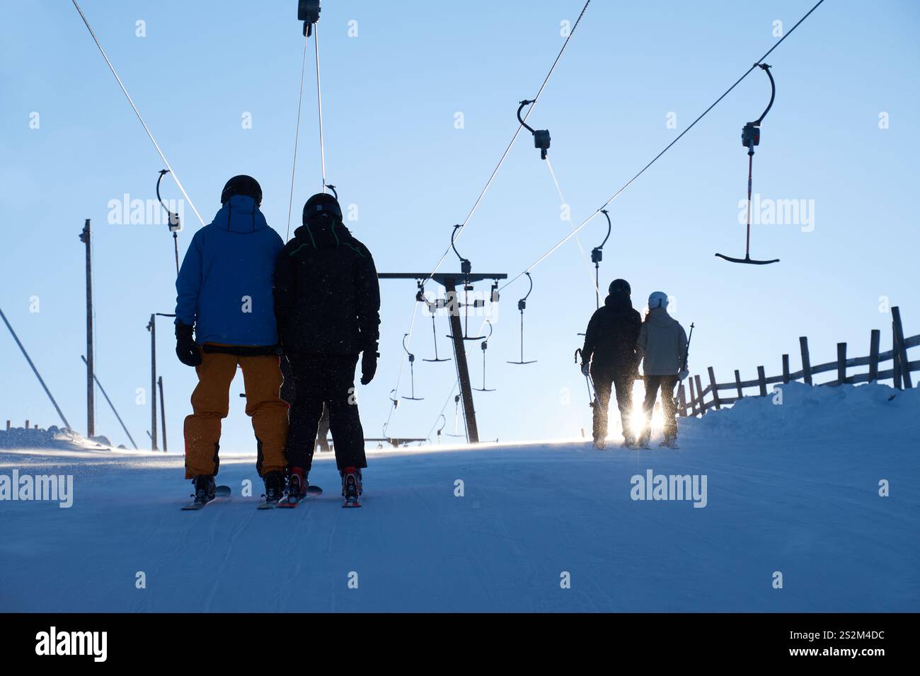 Persons riding a t-bar lift upwards a skiing slope in a winter ...