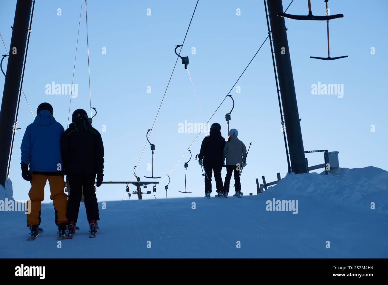 Persons riding a t-bar lift upwards a skiing slope in a winter ...