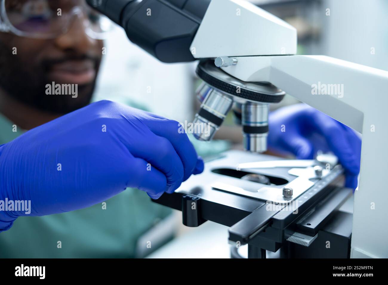 African American male scientist in lab using lens of microscope for ...