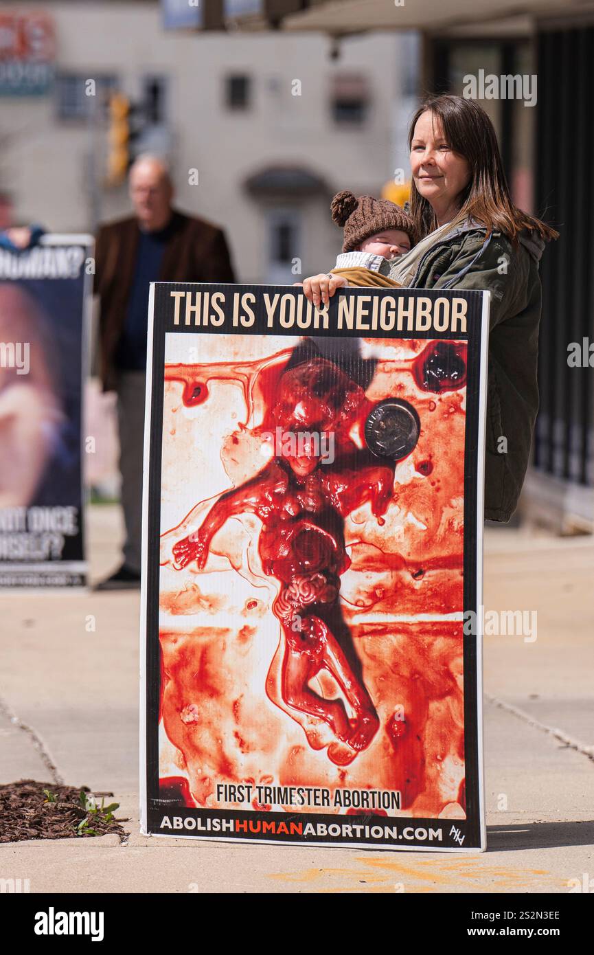 A young woman holding a baby displays a pro-life sign with a bloody ...
