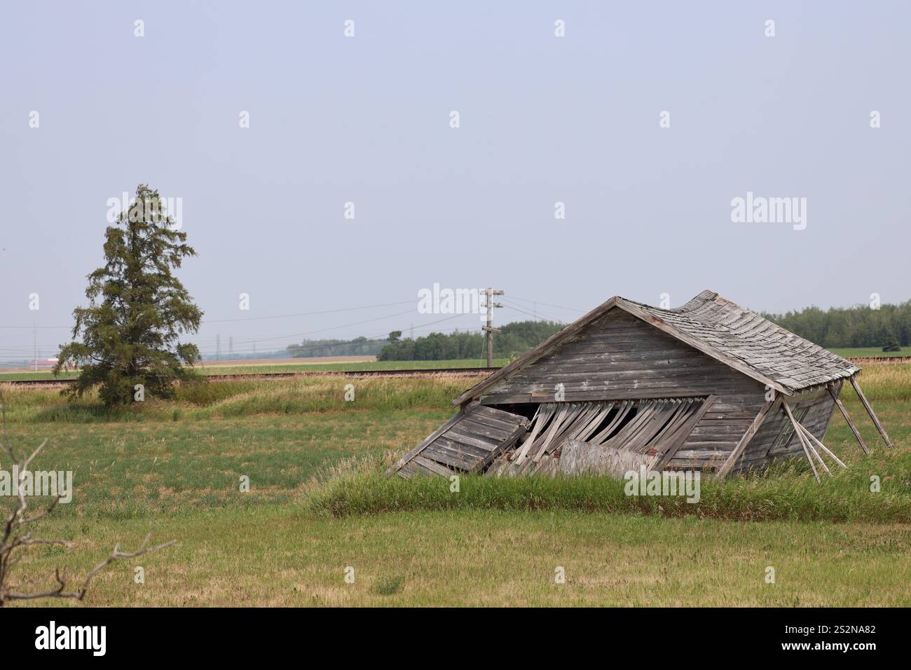wide-angle rustic abandoned farm building propped up on boards in field ...