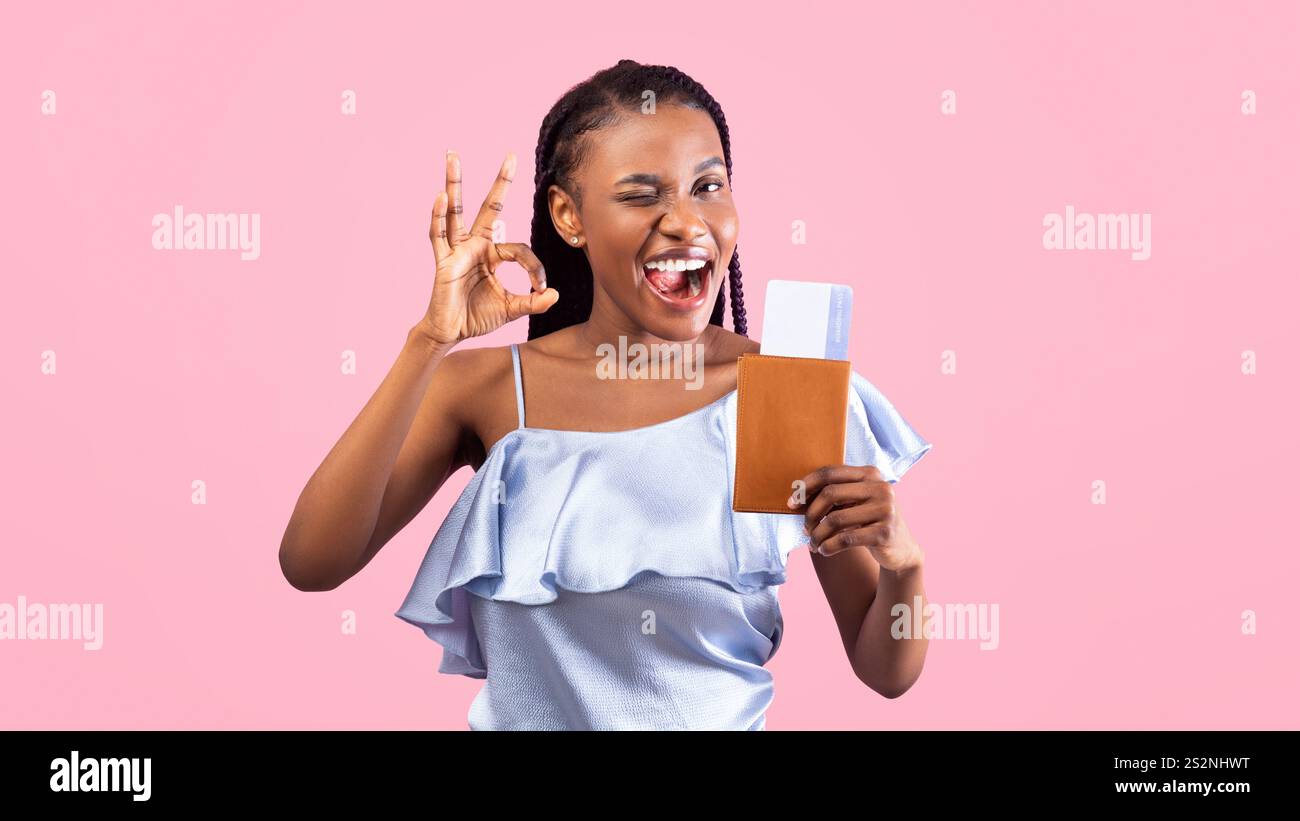 Positive black woman holding passport and plane tickets, showing okay ...
