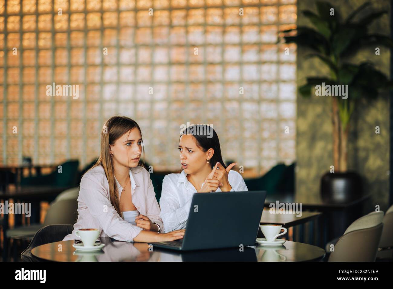 Two college girls are sitting in a cafe and working on a project while ...