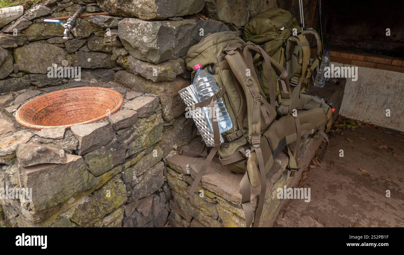 Camping backpacks with water bottles and gear placed on a rustic stone ...