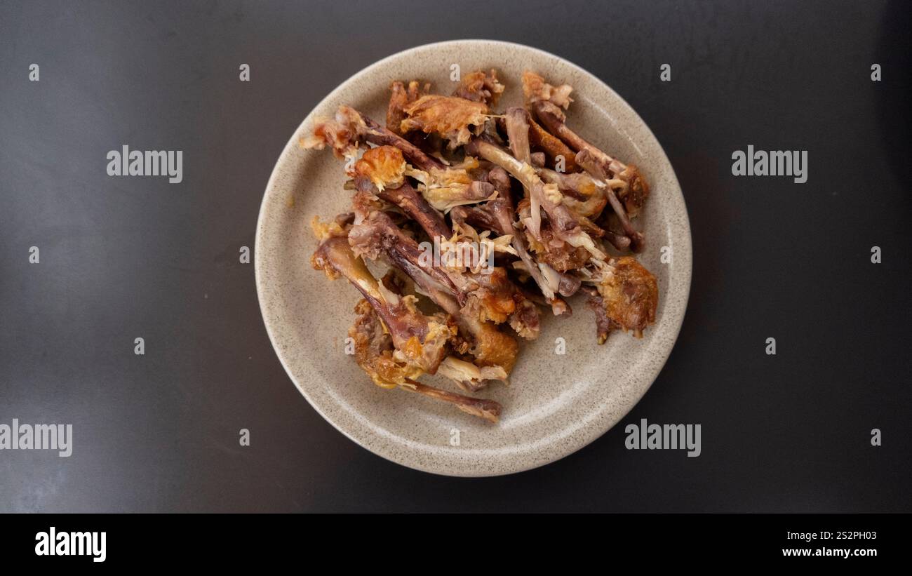 A top-down view of a plate filled with leftover chicken bones on a dark ...
