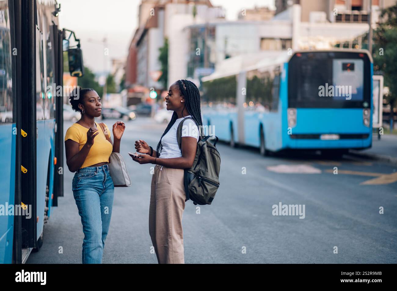 African female young friends waiting at a bus stop and talking ...
