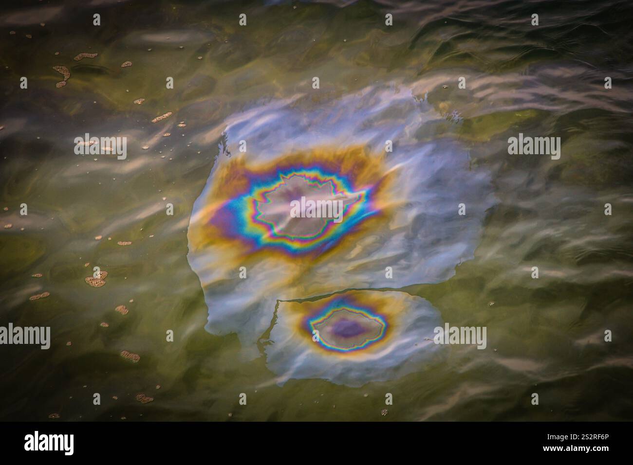 A body of water with a rainbow-colored oil slick on top. The water is ...