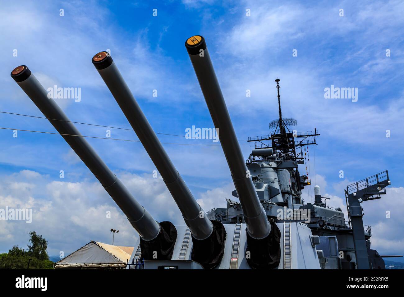 A large battleship with three large guns on the front. The sky is blue ...