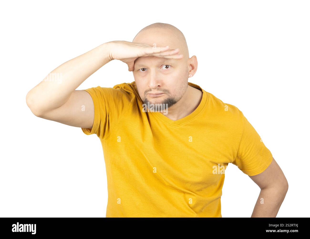 A bald man with a beard is wearing a yellow shirt and shading his eyes ...