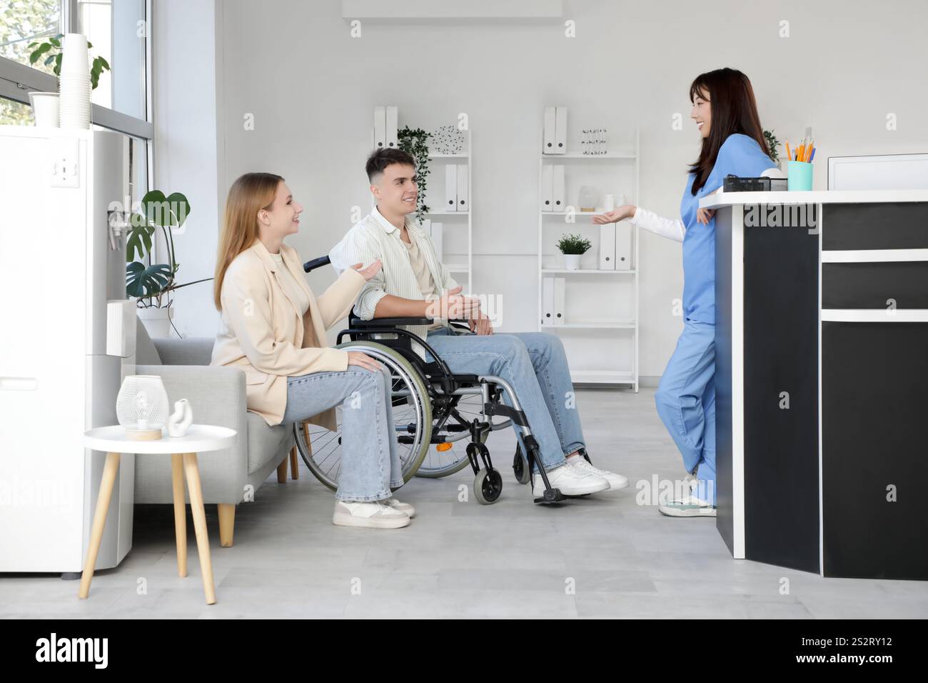 Female Asian medical intern working with man in wheelchair and woman at ...