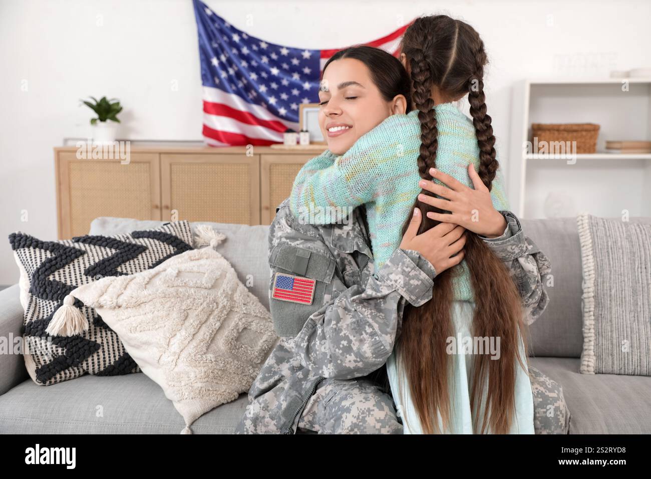 American female soldier hugging her daughter on sofa at home Stock ...