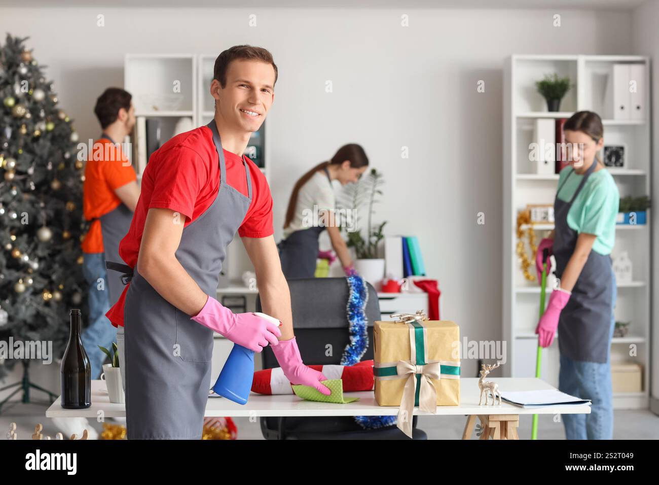 Male janitor cleaning table and his team in office after New Year party ...