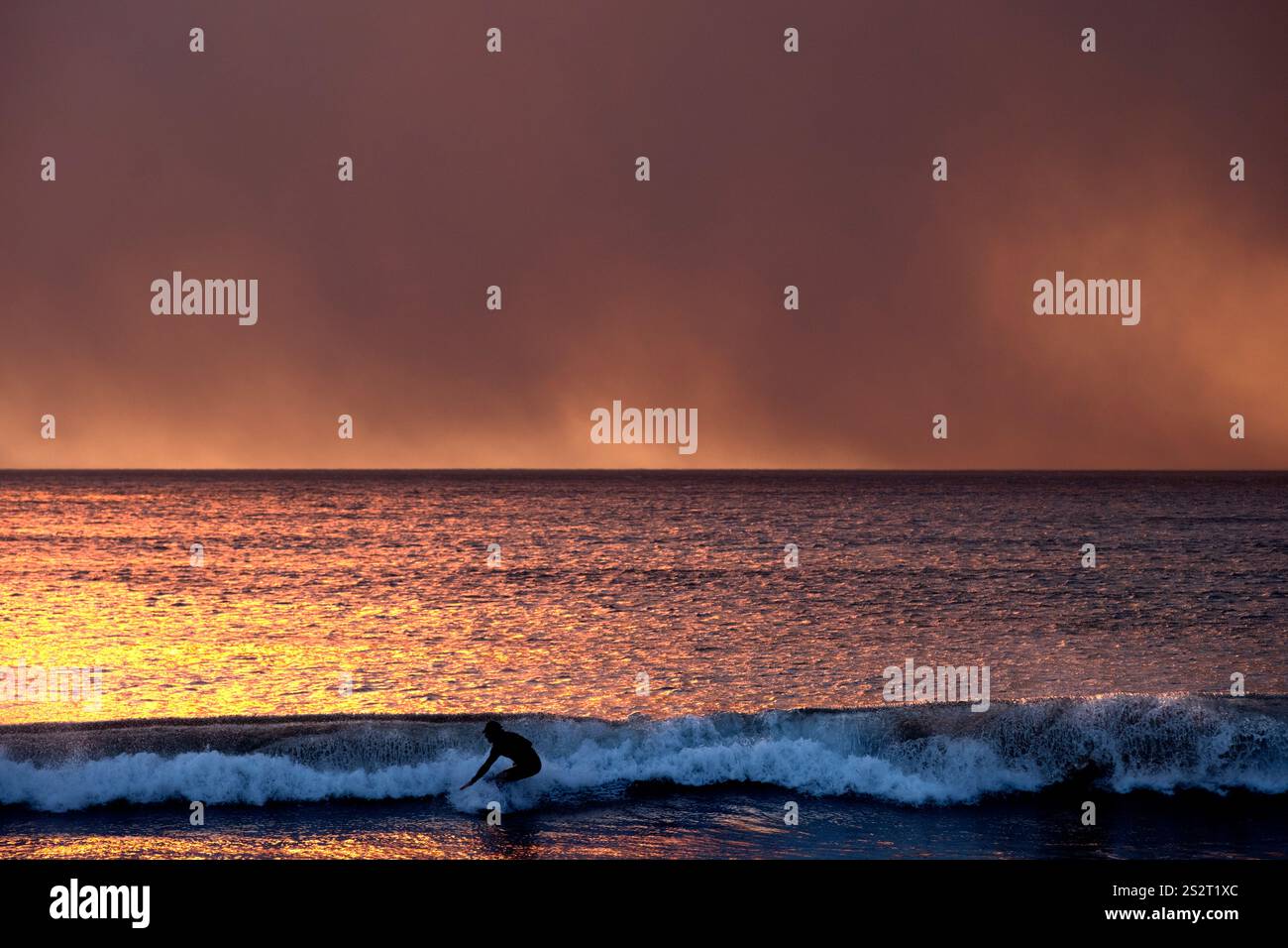 A surfer takes off on a wave under a blackened sky from the Palisades ...