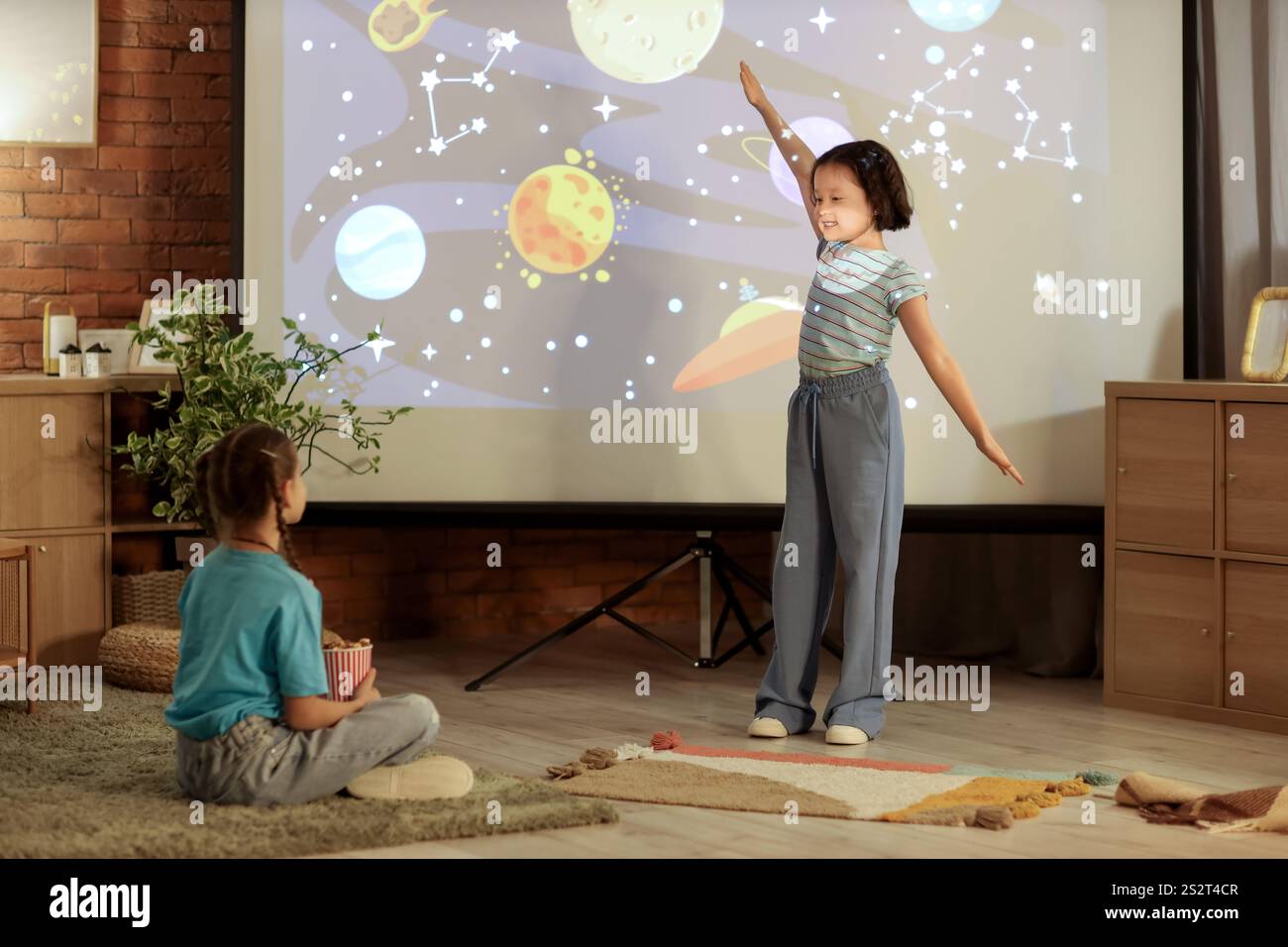 Cute girls watching cartoons on projector screen at home in evening ...