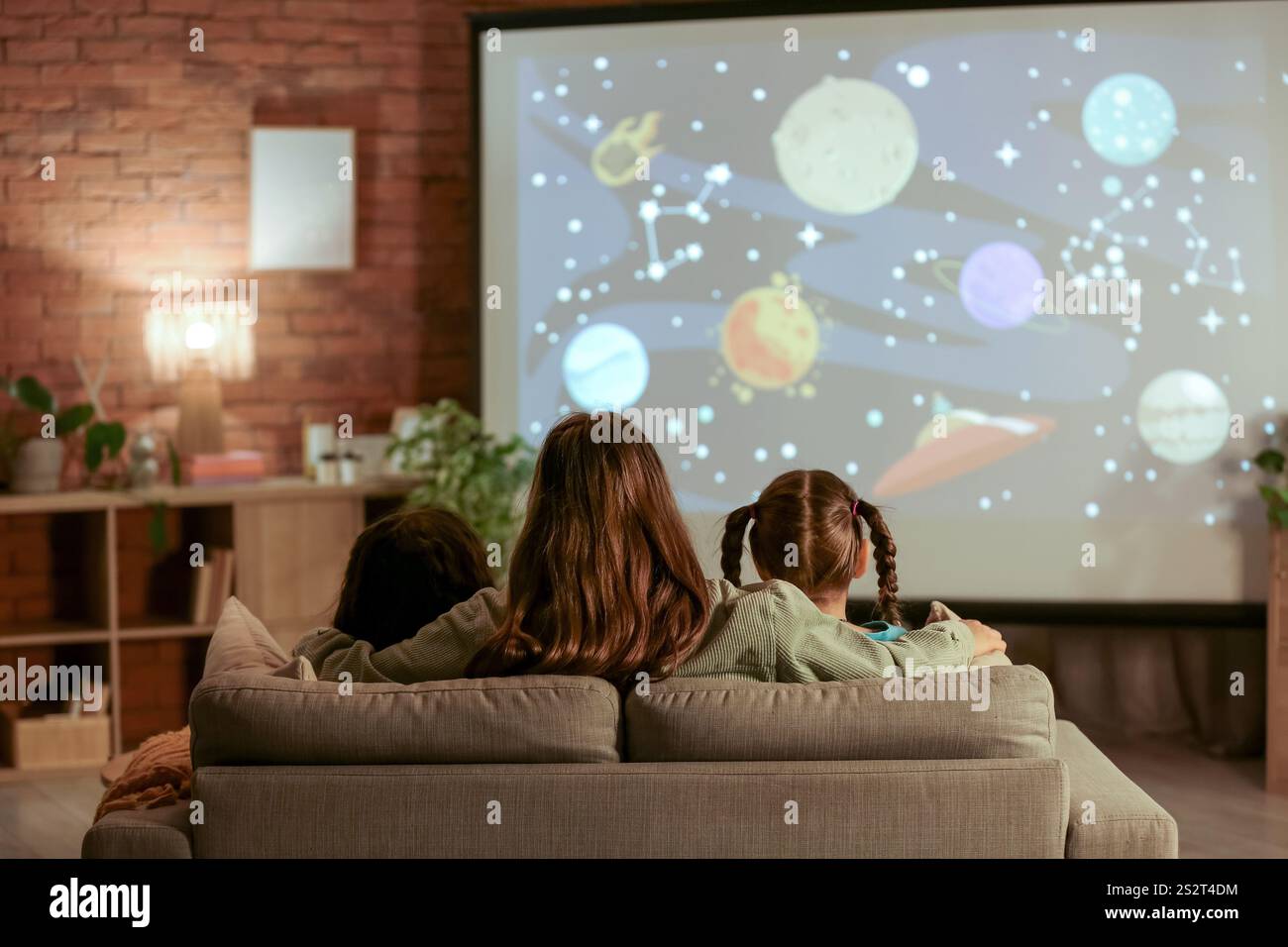 Cute girls with their mother watching cartoons on projector screen at ...