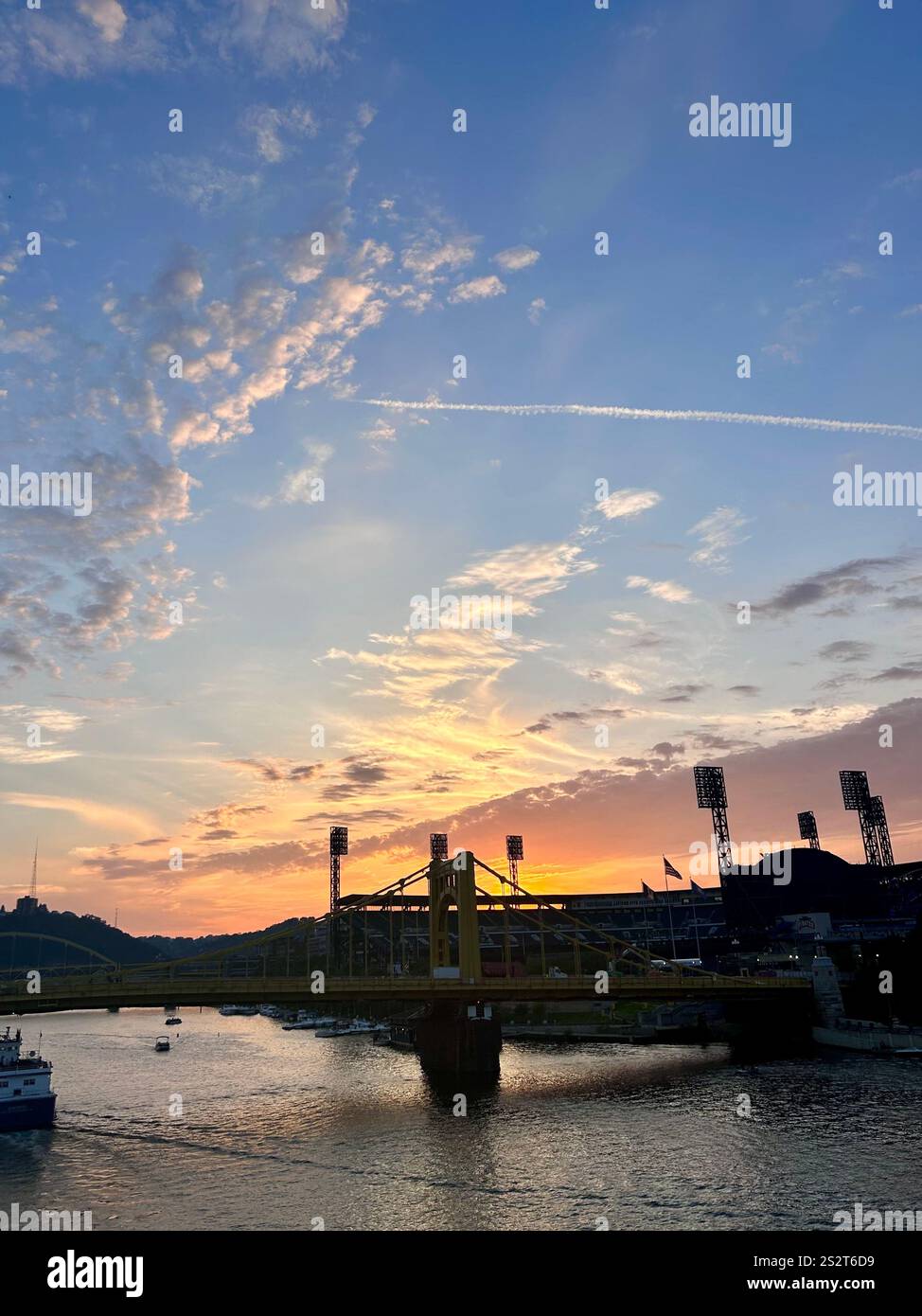 Setting sun over city river, bridges, and stadium Stock Photo - Alamy