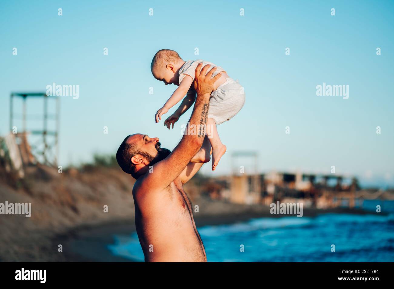 Wide shot of a happy father at the beach throwing his smiling son into ...