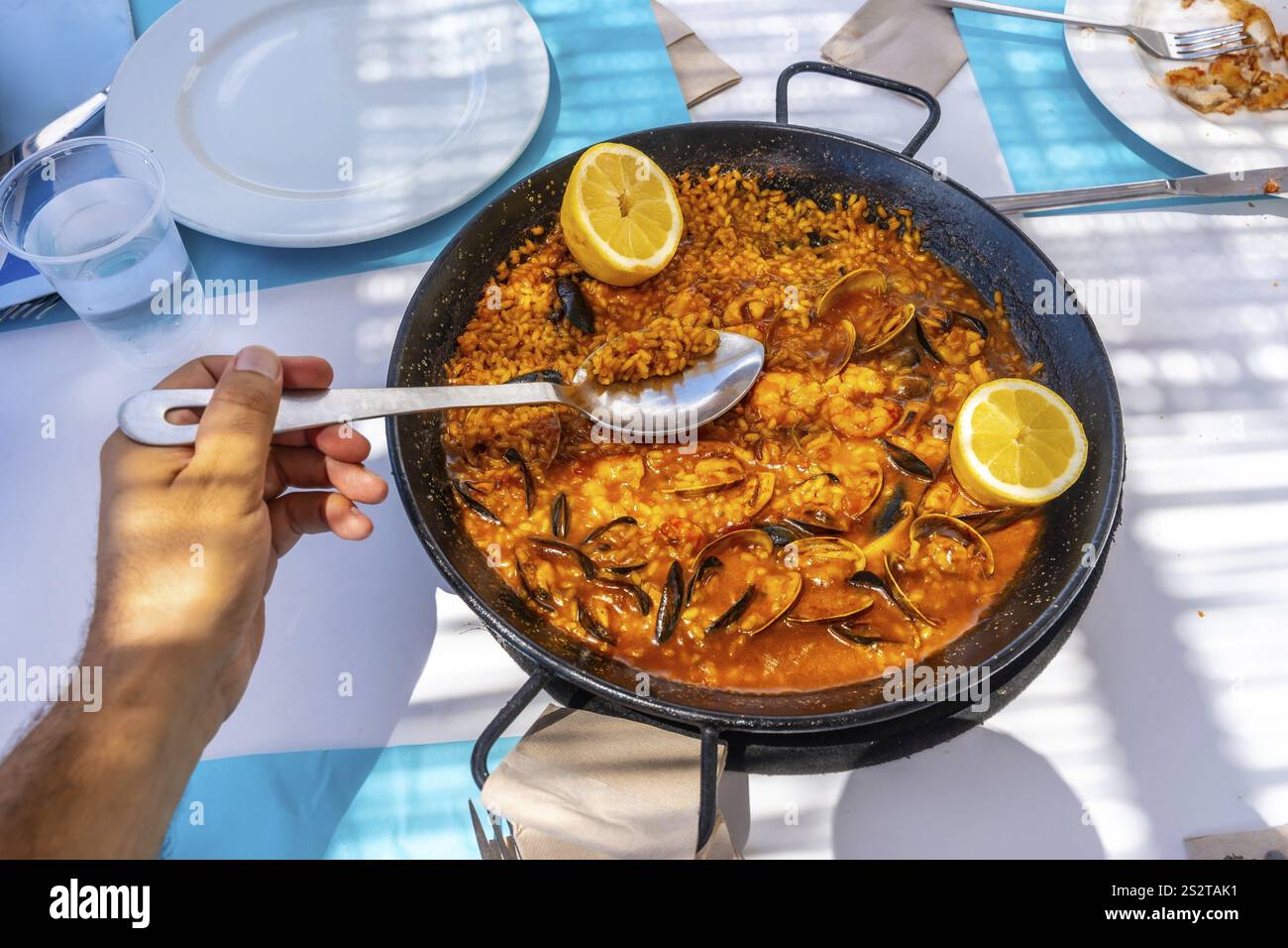 Hand holding spoon scooping seafood paella from pan in outdoor ...
