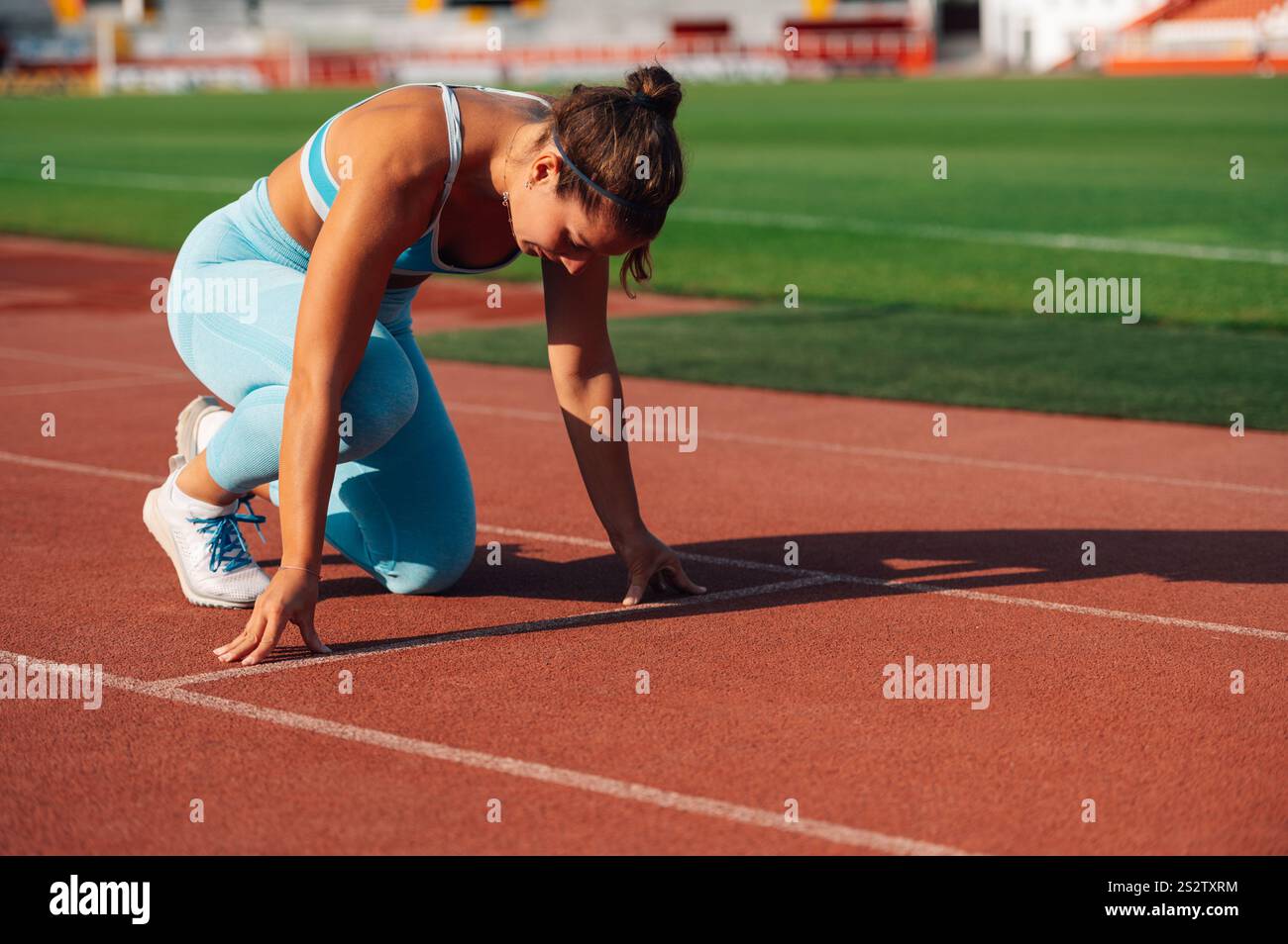 A sporty female athlete in start position on running track on stadium ...