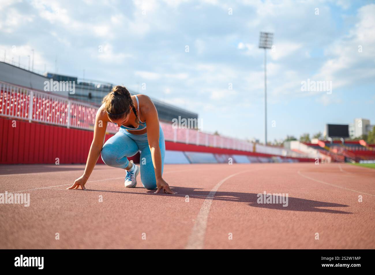A female track runner in start position on running track preparing for ...