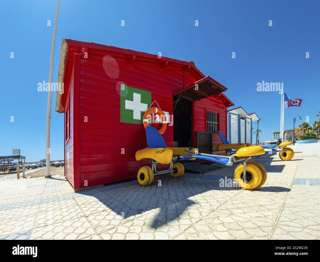 Floating wheelchairs parked outside a red lifeguard station on a sunny ...