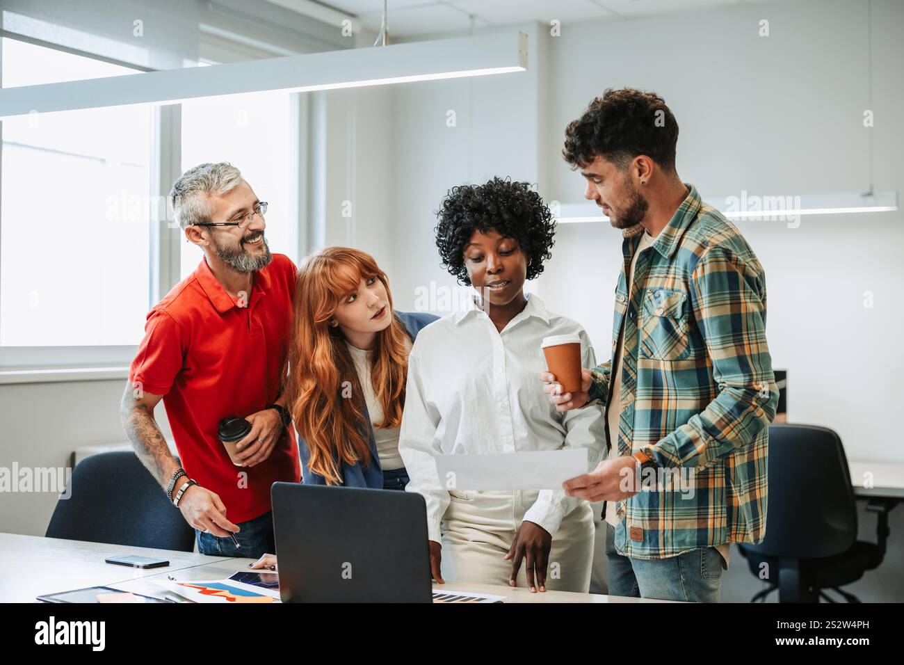 Diverse happy colleagues using laptop and discussing work and drinking ...