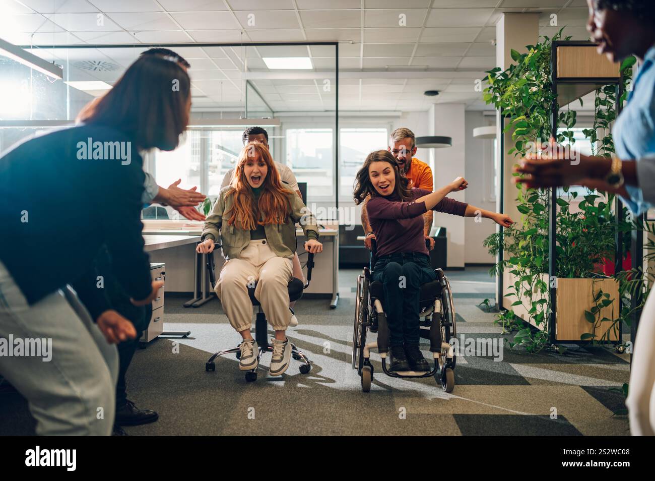 Four young coworkers enjoying office chair race at workspace and having ...