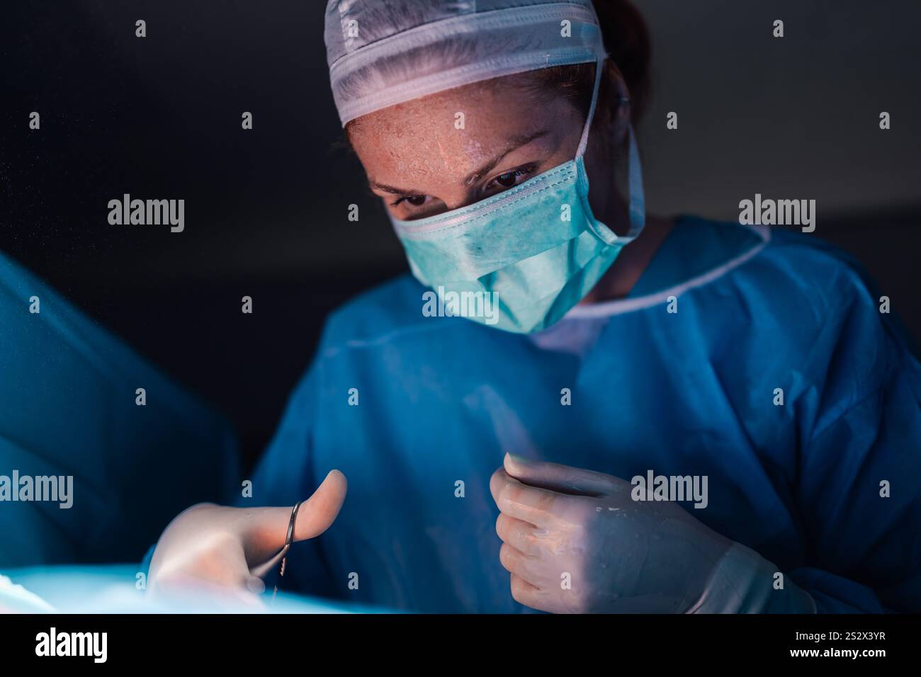 A surgeon dressed in a blue surgical gown and gloves, concentrating on ...