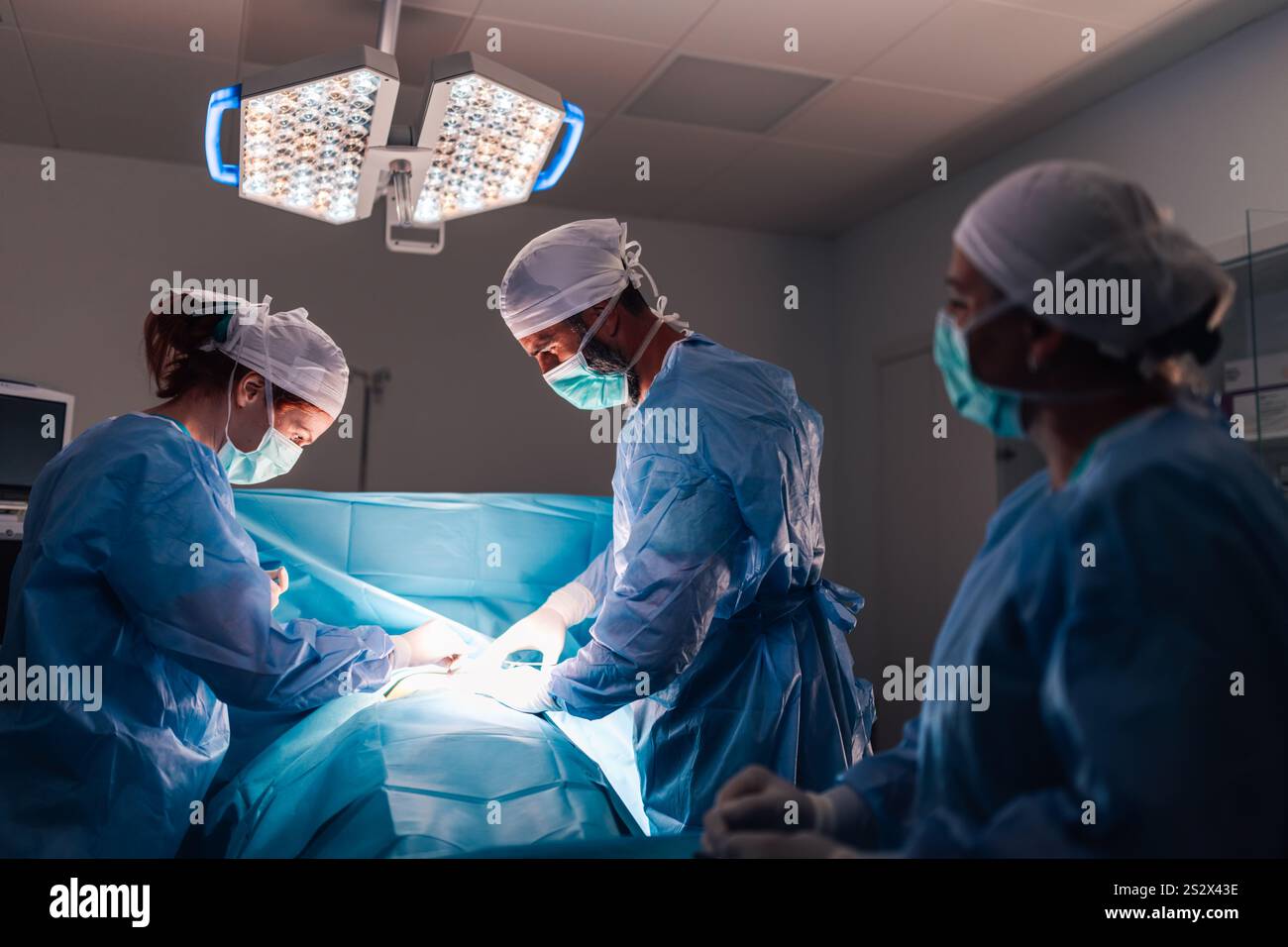 A group of doctors in surgical attire perform a surgery in a modern ...