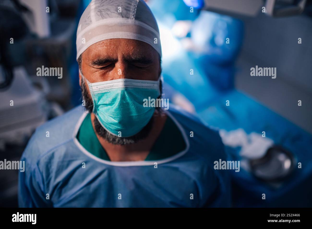 A surgeon, geared in blue surgical gown and cap, stands ready to ...