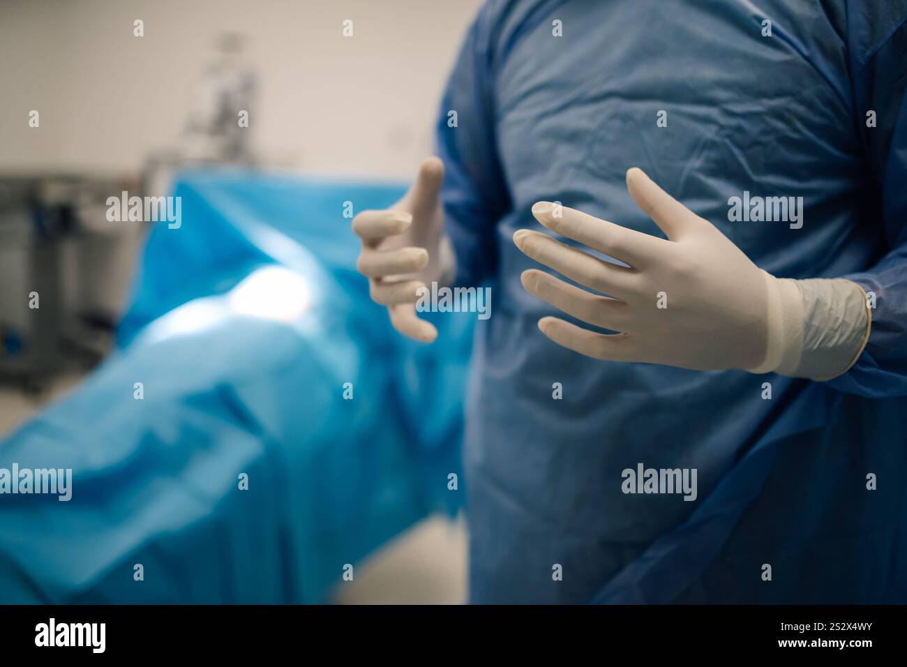 A surgeon wearing blue scrubs and sterile gloves prepares for a ...