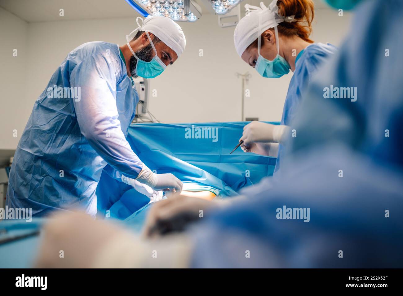 A surgical team in bright blue attire and gloves, performing an ...