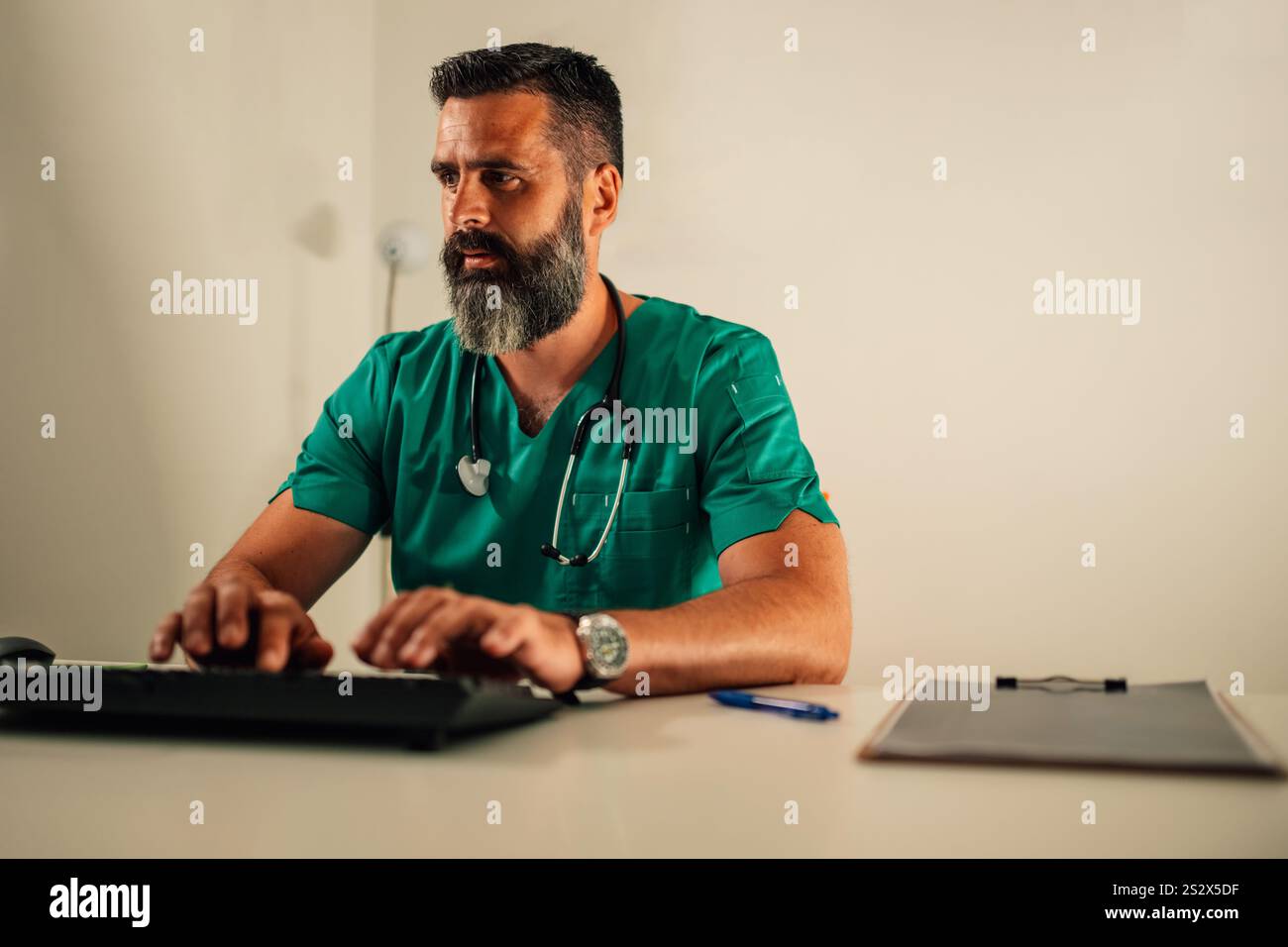 A doctor dressed in green scrubs is actively typing on a computer ...
