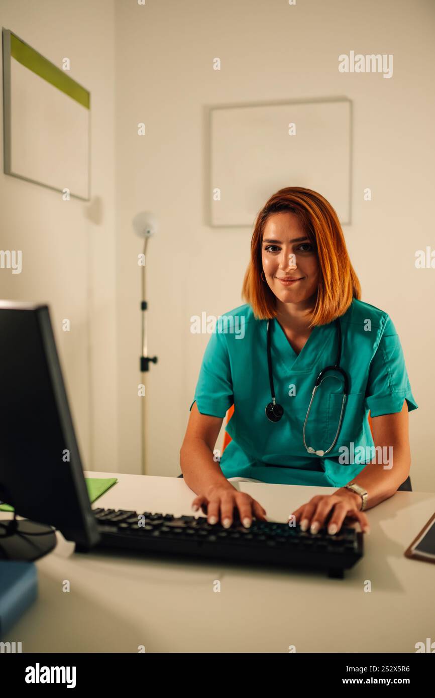 A young female doctor in green scrubs confidently smiles as she works ...