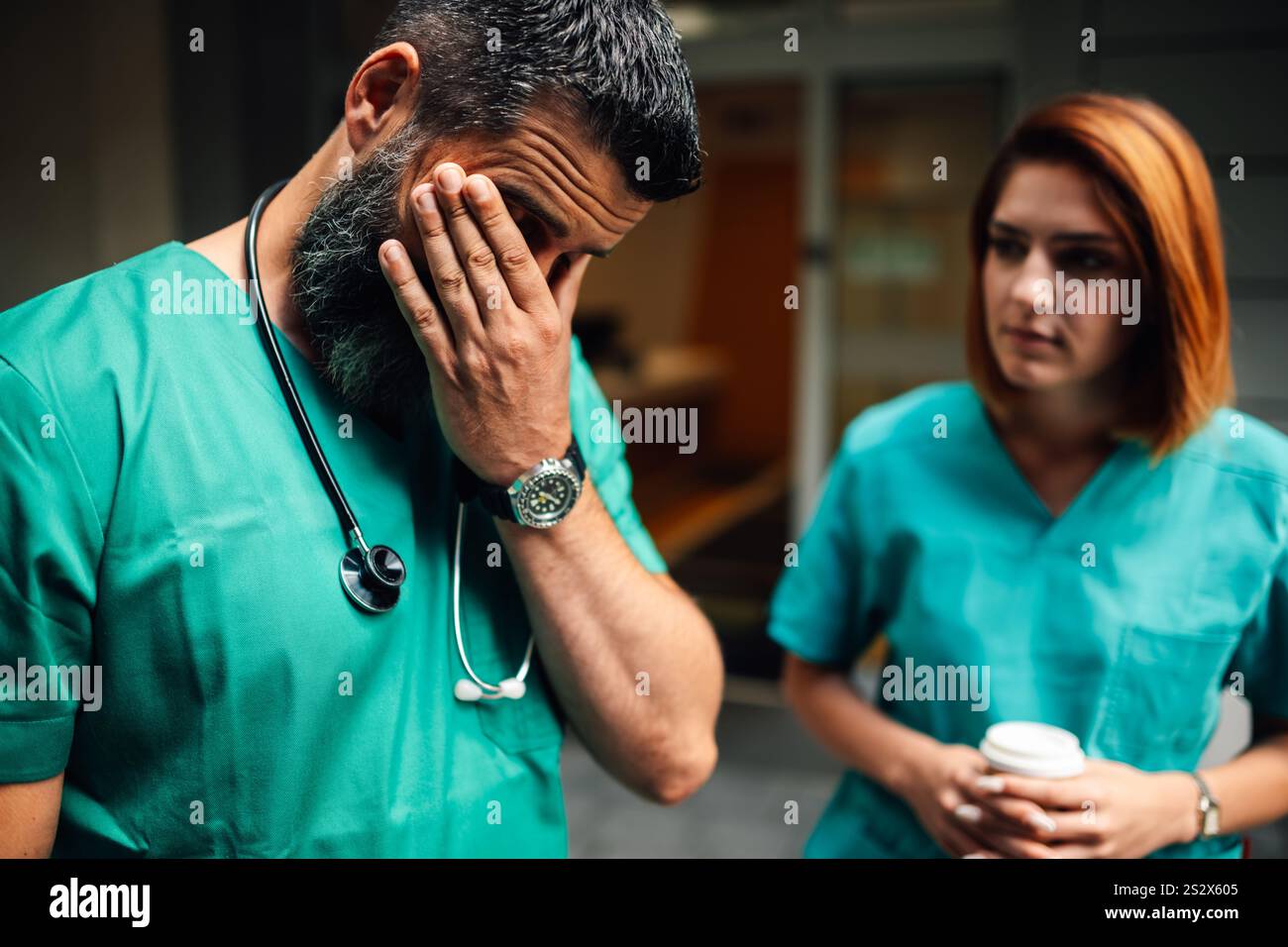 A male doctor shows signs of distress, touching his face with one hand ...