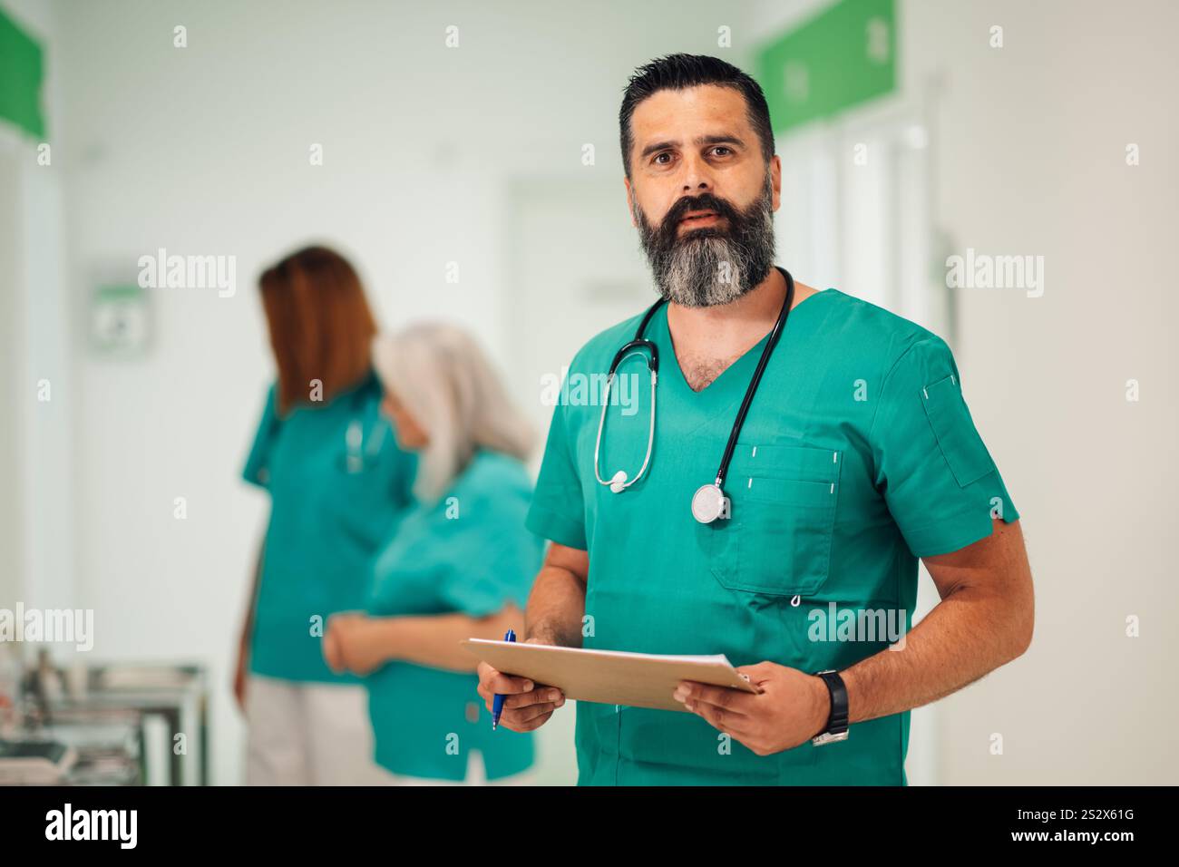 A dedicated male nurse with a beard, wearing green scrubs, stands ...
