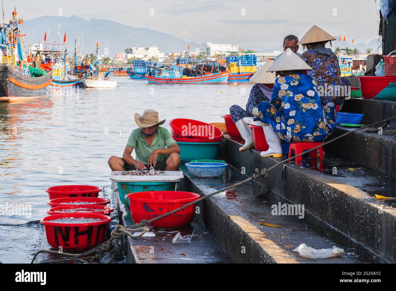 Vietnamese women sit on the steps of the seaport and sell fresh fish ...