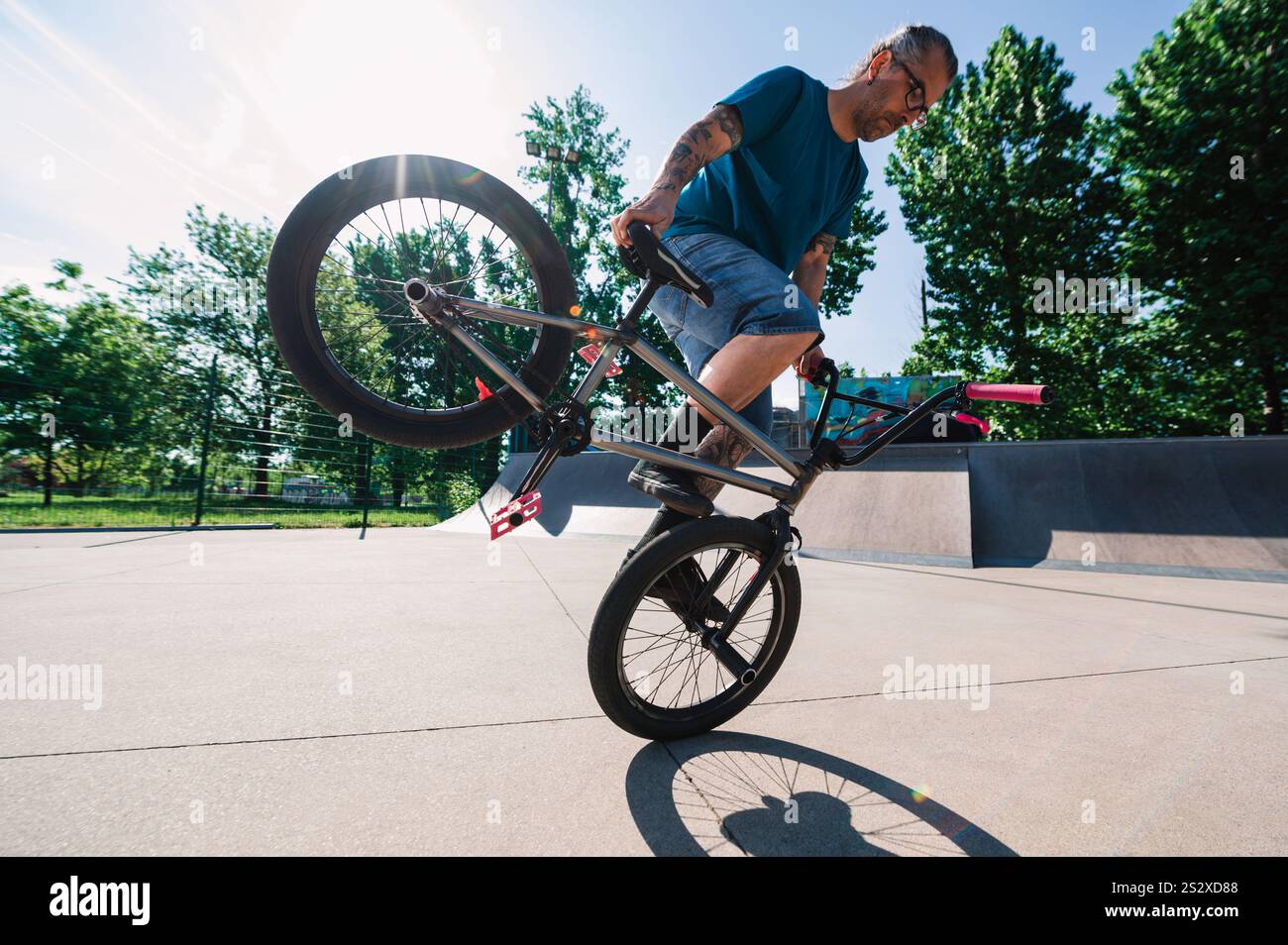 A middle-aged urban tattooed guy is standing on one wheel on his bmx ...