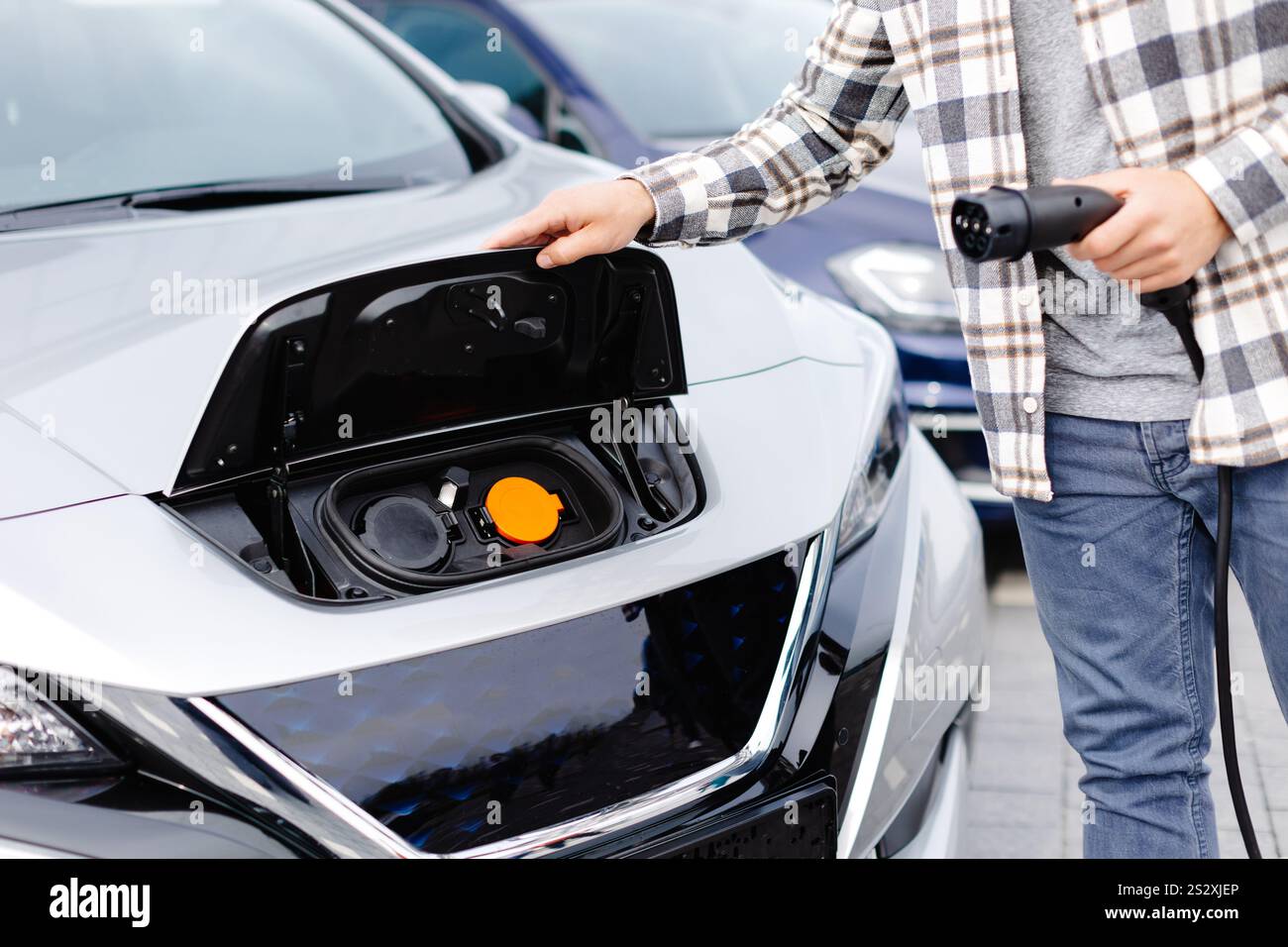 Young man plugging charging cable into the car socket. Electric car ...