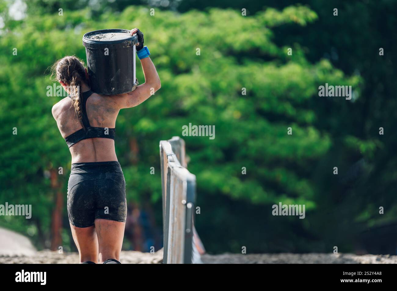 Rear view of a fit sportswoman carrying a heavy barrel resting on her ...