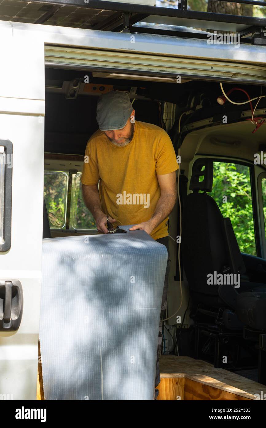 Skilled craftsman upholstering a seat inside his campervan ...