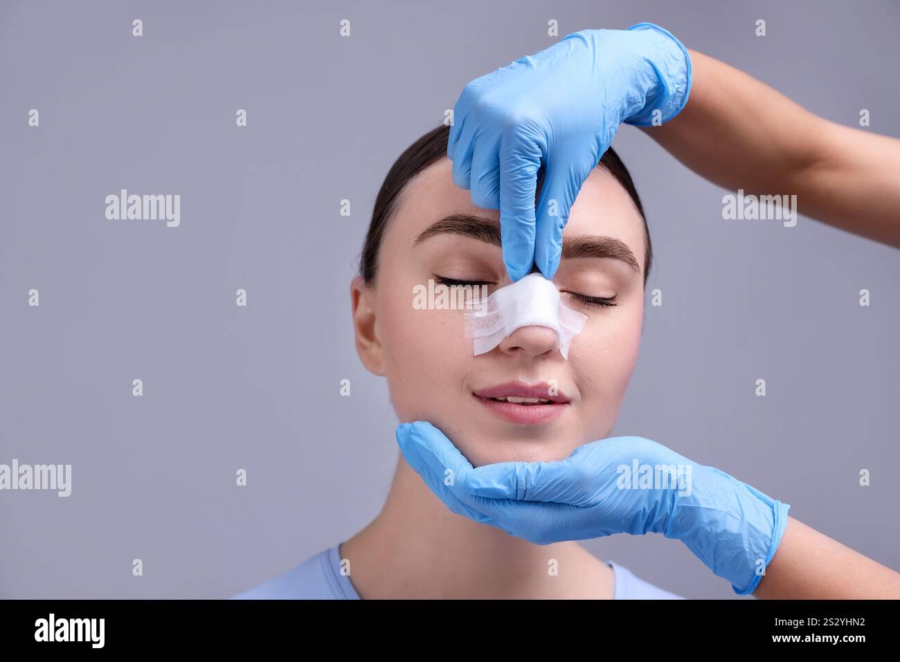 Doctor checking patient's nose after plastic surgery operation on grey ...