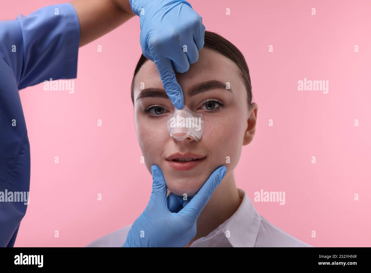 Doctor checking patient's nose after plastic surgery operation on pink ...