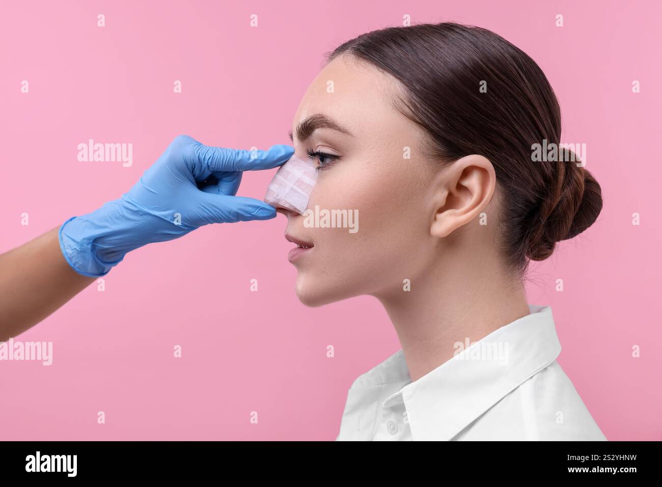 Doctor checking patient's nose after plastic surgery operation on pink ...