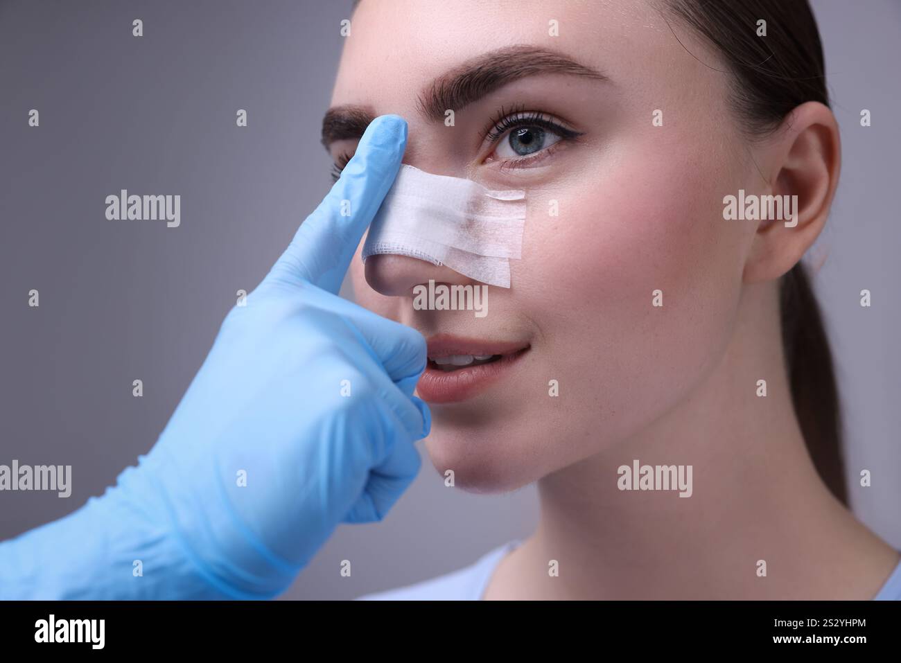 Doctor checking patient's nose after plastic surgery operation on grey ...