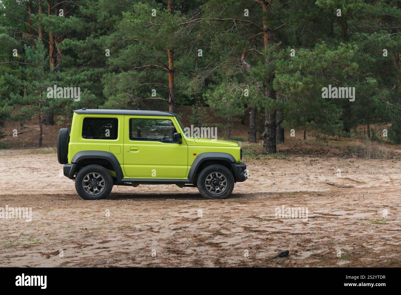 Lime green Suzuki Jimny in pine forest. Side view of off-road mini SUV ...