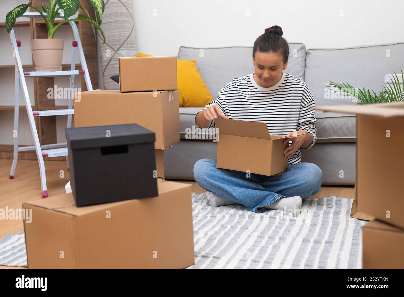 Brunette lady with delighted expression sits on floor with box Stock ...