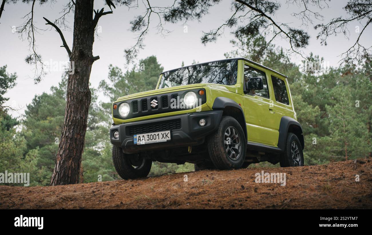 Lime green Suzuki Jimny in pine forest. Three quarter front view of off ...