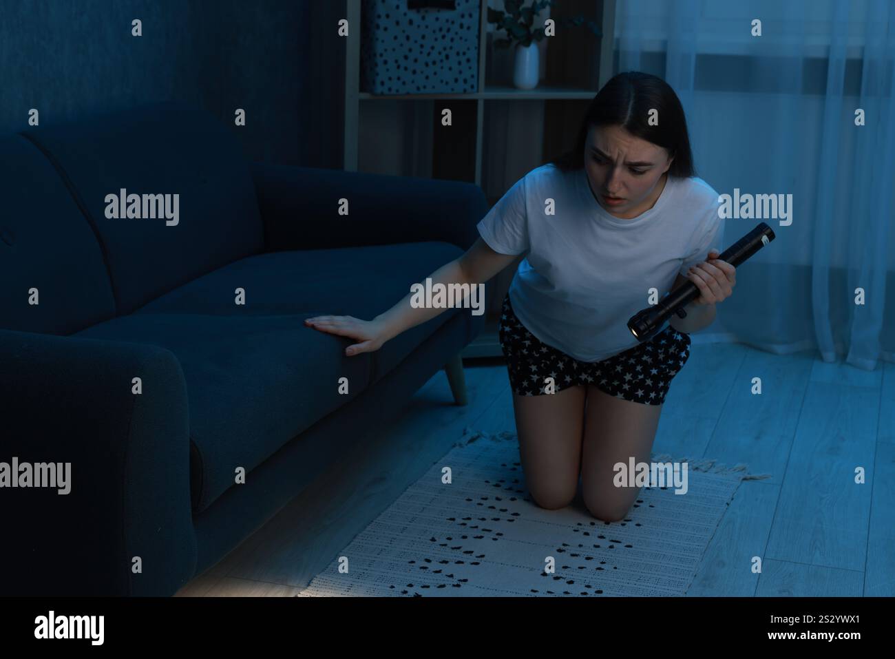 Fear of darkness. Scared young woman looking under couch with ...