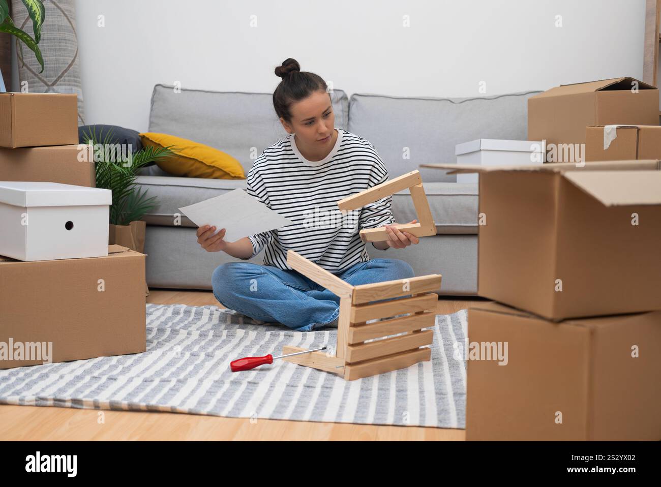 woman self-assembly shelf in new house, surrounded by moving carton ...